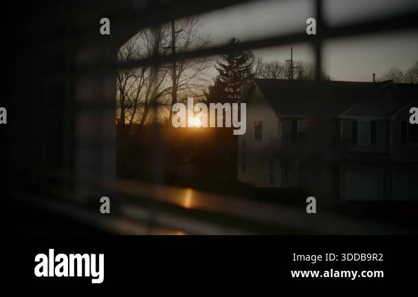 Warm sunset light shines through partially closed window blinds ...