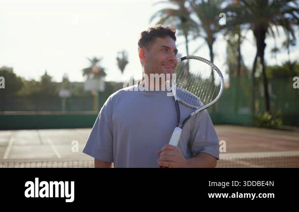 Young athletic man standing on outdoor tennis court holding racket ...