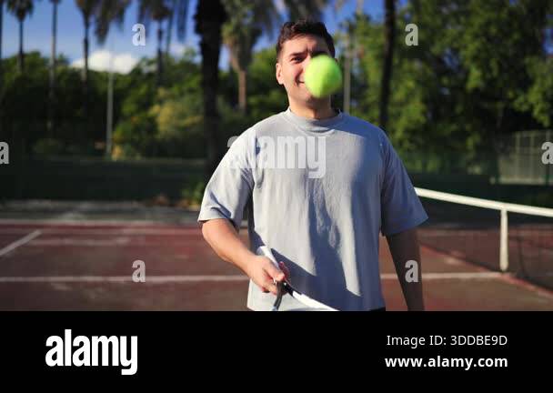 Male tennis player tossing ball with racket on outdoor court, relaxed ...