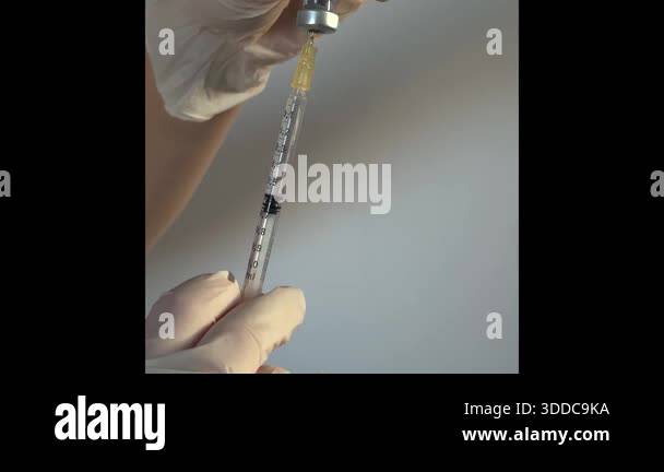 Doctors gloved hands meticulously drawing a yellow liquid medication ...