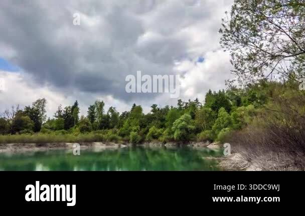 Timelapse of clouds drifting over a serene green forest lake with ...
