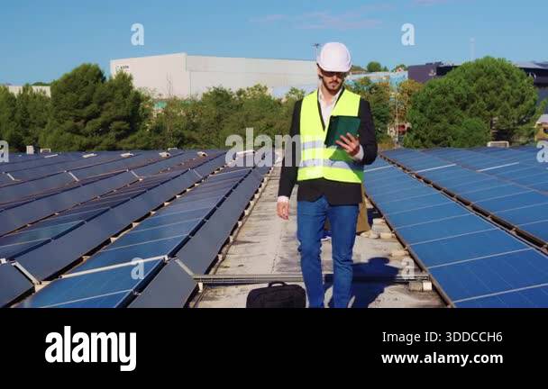 Male renewable energy engineer in a safety vest and hard hat walking ...