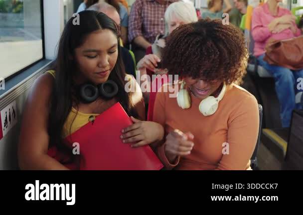 Two diverse female friends sitting together on public transport ...