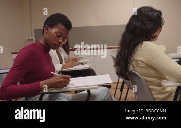 Group of multiethnic university students attentively writing in their ...