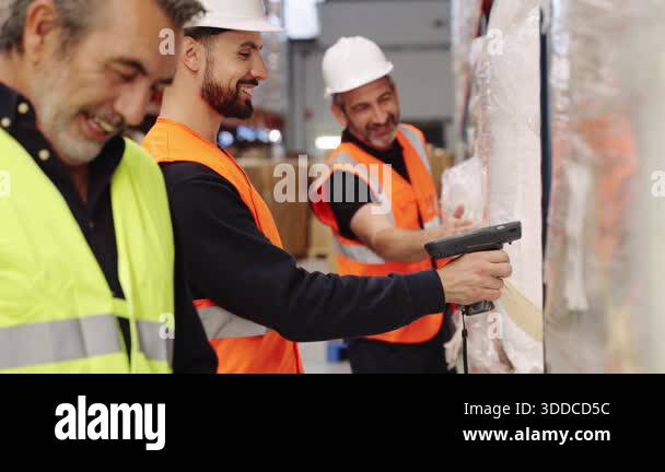 Three smiling male workers in a distribution warehouse using a barcode ...