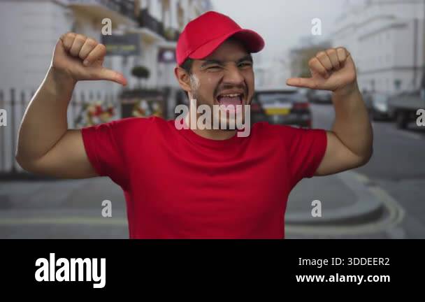 Hispanic man pointing thumbs to chest on busy street under red cap ...