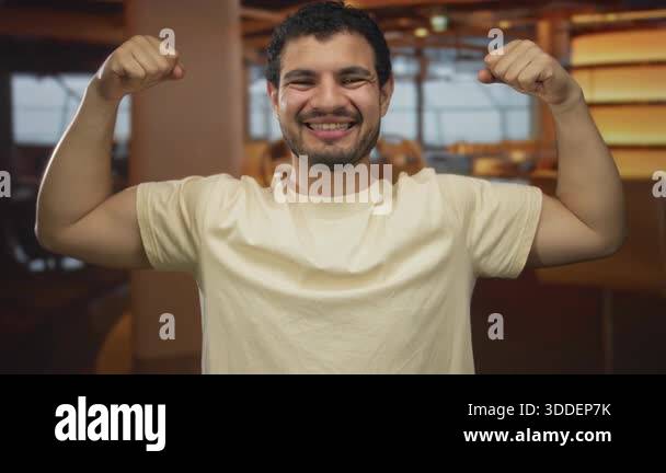Man flexes arms in a building restaurant hall wearing a white t shirt ...