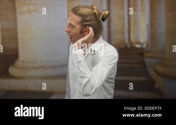 Man cups hand to ear in building ruins surrounded by towering stone ...