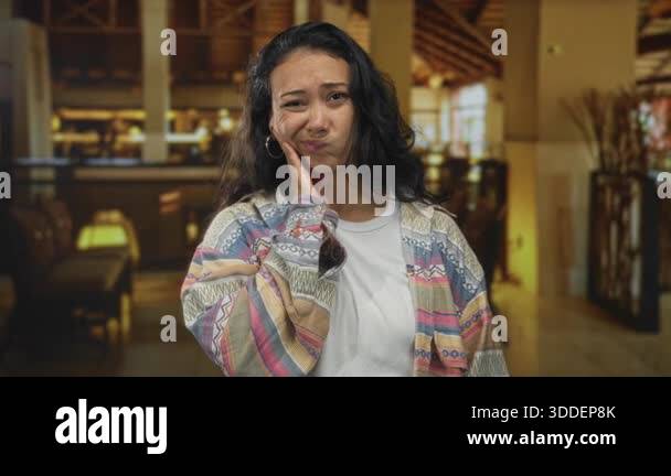Woman pressing cheek with hand inside hotel building, wincing in ...