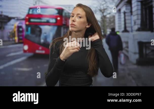Woman hand to chin and flipping hair beside red doubledecker bus on ...
