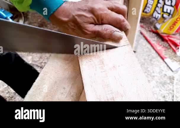 Carpenter hand cutting wooden plank with sharp metal saw blade during ...
