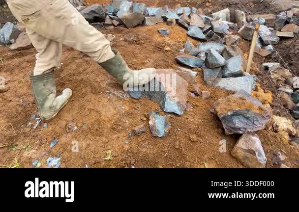 Close-up of a worker wearing boot breaking large rock with a hammer on ...