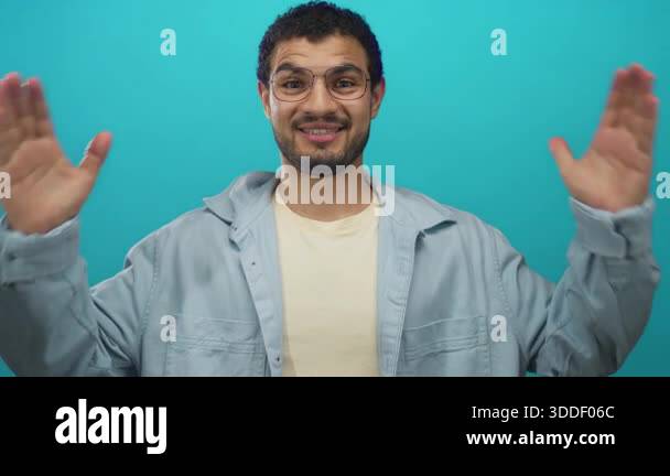 Bearded man with glasses holds up hands against turquoise wall in ...