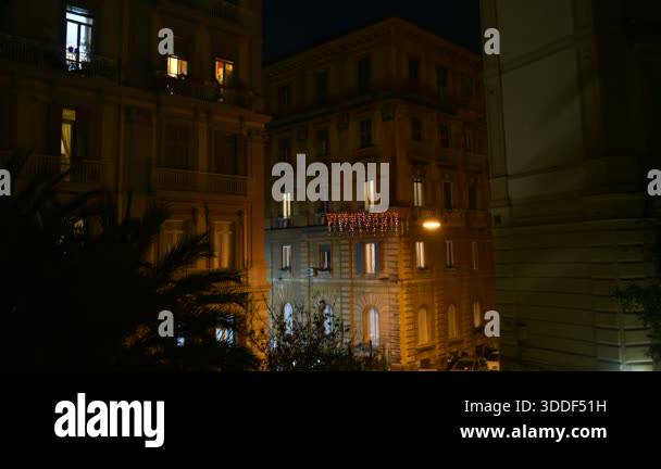 People moving inside illuminated windows of an old building at night ...