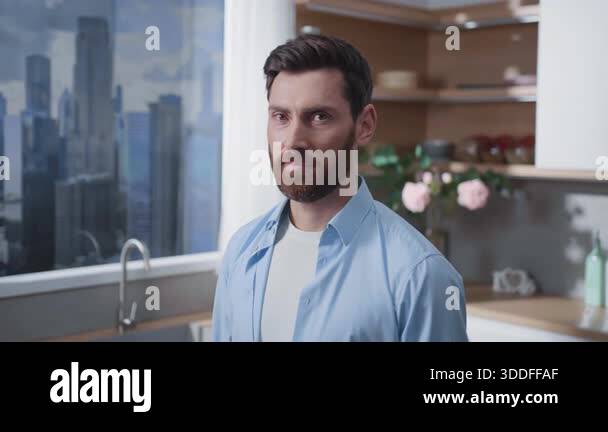 A thoughtful man stands in a sleek, modern kitchen, gazing out at the ...