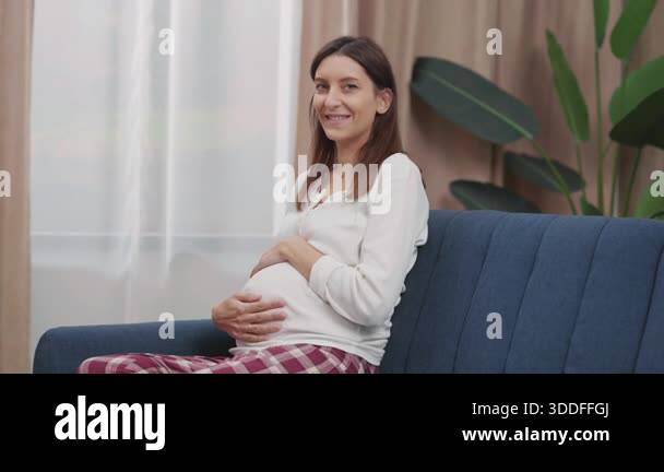 Caucasian pregnant woman smiling cheerfully at camera, gently hugging ...