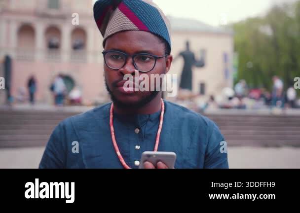 A young man, wearing traditional attire, engages with his smartphone ...