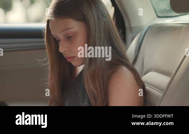 Good-looking little girl sitting at backseat, looking down. Close-up ...
