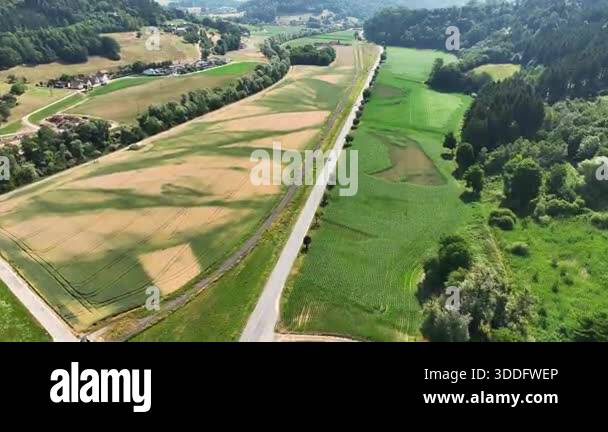 Aerial summer footage of bright fields with crops, winding rural road ...