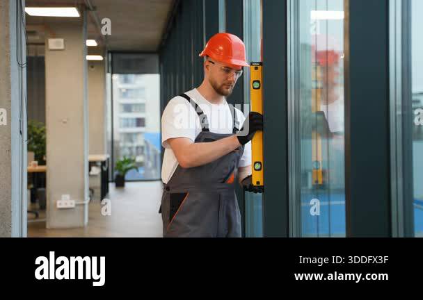 Professional builder in a hard hat and overalls using a spirit level to ...