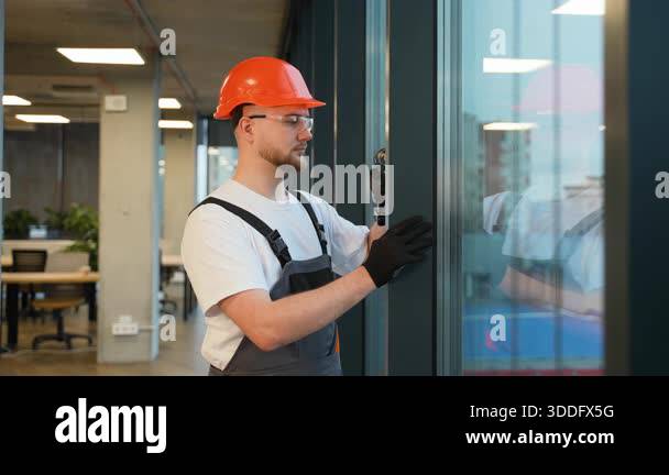 Male builder in a hard hat and protective glasses performing window ...