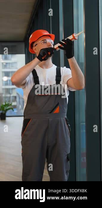 Professional builder in a hard hat and overalls using a caulking gun ...