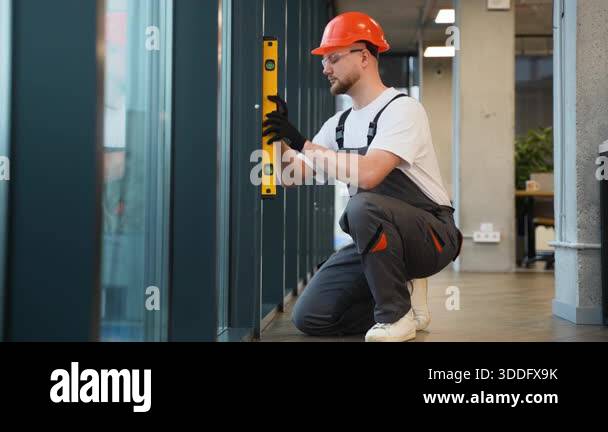 Male builder in a hard hat and uniform using a spirit level tool to ...