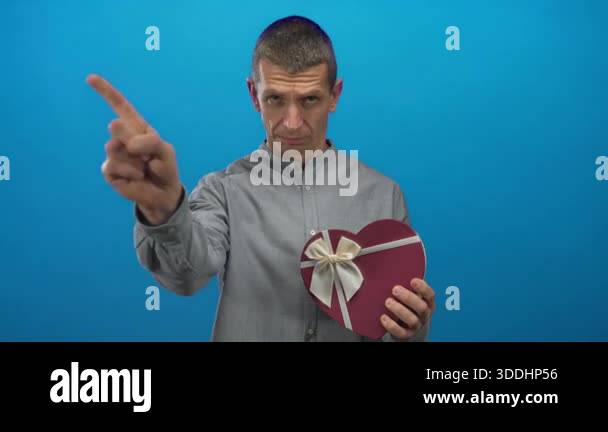 Man holding a heart-shaped gift box while gesturing no with a finger ...