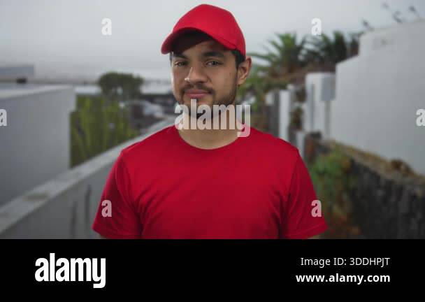 Man wearing red shirt and cap makes air quotes gesture on a street ...