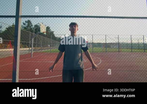 A teenage boy leans against a sports field fence, deep in thought ...