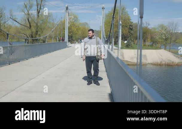 A homeless man walks alone across a pedestrian bridge carrying a ...