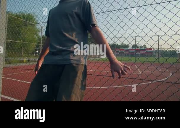 A teenager leans back against a sports fence, looking serious and ...