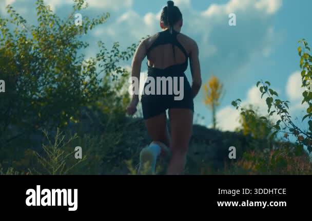 Captured from below, a woman in sporty outfit runs up a hill trail ...