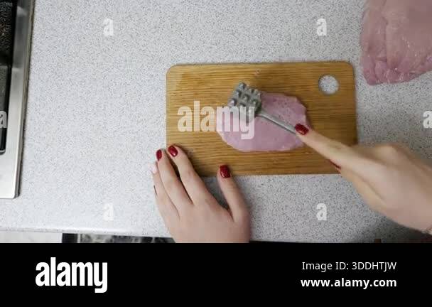 Womans hands with red nails use a meat mallet to pound a raw pork loin ...