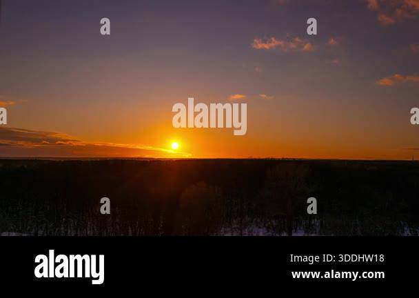 Sun sets over a dark treeline, casting a golden glow on the horizon ...