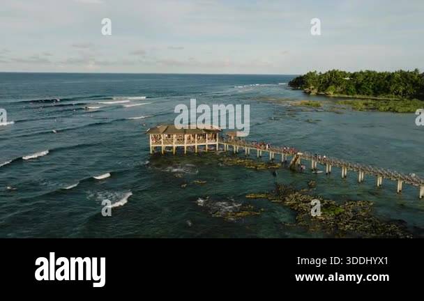 Wooden hut on pier surrounded by waves breaking on reef and surfers in ...