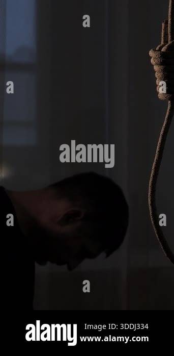 A rope noose hangs in a dark apartment. The man is depressed and upset ...