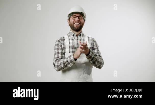A cheerful builder in white overalls and a hard hat claps his hands and ...