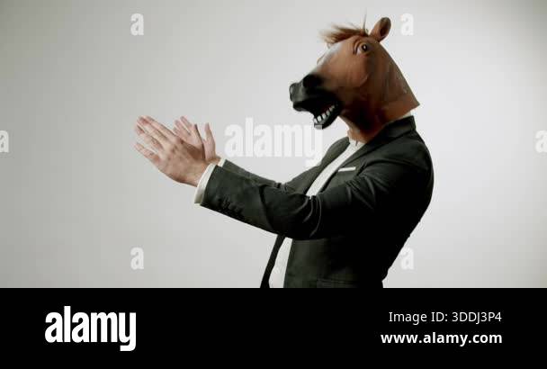 A man in a suit dances while wearing a horse mask against a white ...