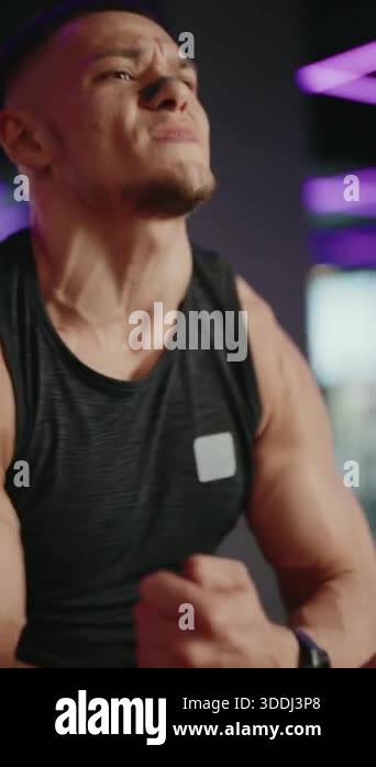 A muscular man flexes his biceps in a gym with purple neon lighting. He ...