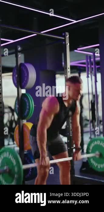 A determined male weightlifter performs repetitions with a barbell in a ...