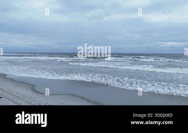 Cold ocean waves rolling onto a deserted sandy beach under a dramatic ...