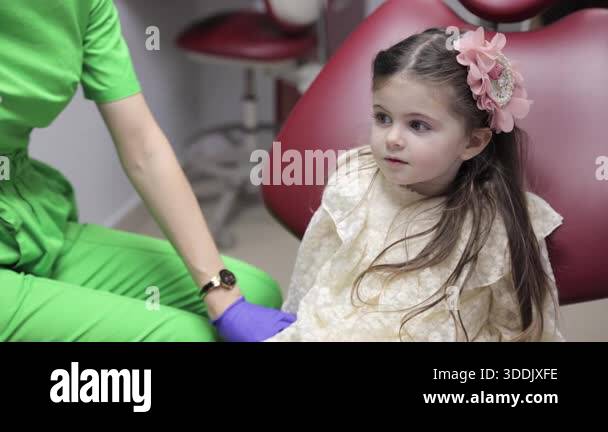Female dentist in a green uniform reassuring a young girl patient ...