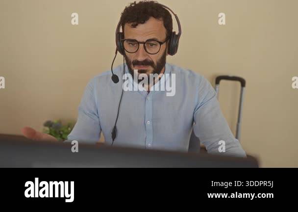 Man with headset in office looking stressed at computer while holding ...
