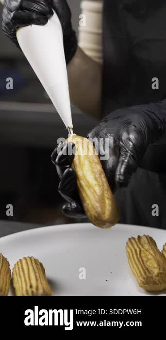 Professional confectioner filling eclairs with custard cream using a ...