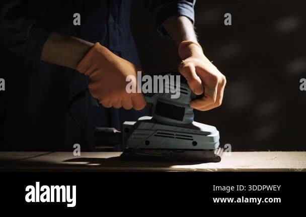 Carpenter sanding wooden board with electric orbital sander in his ...