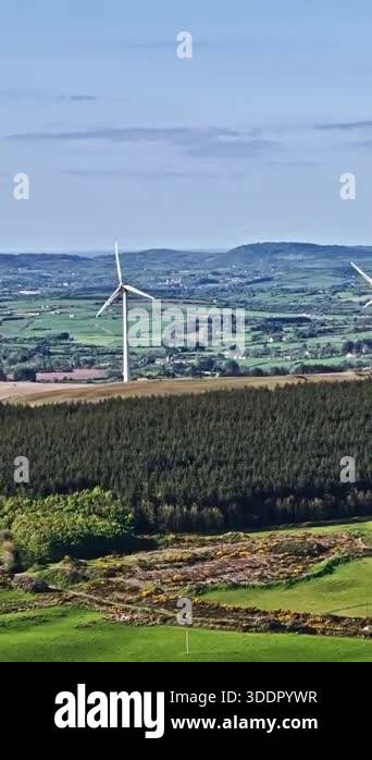 Wind turbines rotate on a hill in Ireland against the backdrop of green ...