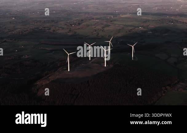 Aerial view shows multiple wind turbines on a hill in Ireland. The sun ...