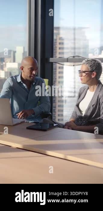 Vertical. A male and female coworker analyze work on a laptop beside a ...