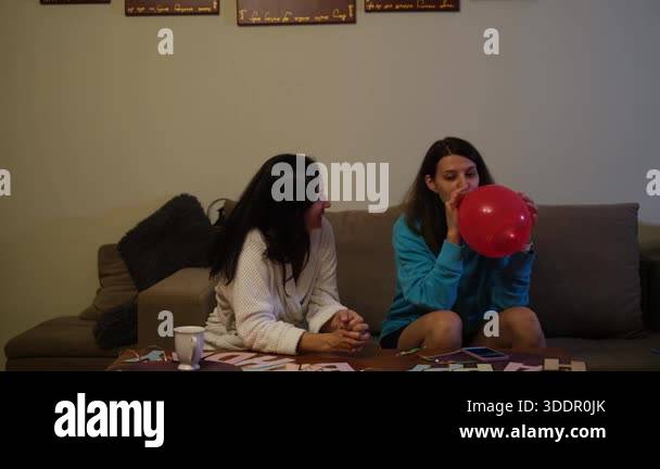 Two friends enjoy their time at home. One friend blows up a pink ...